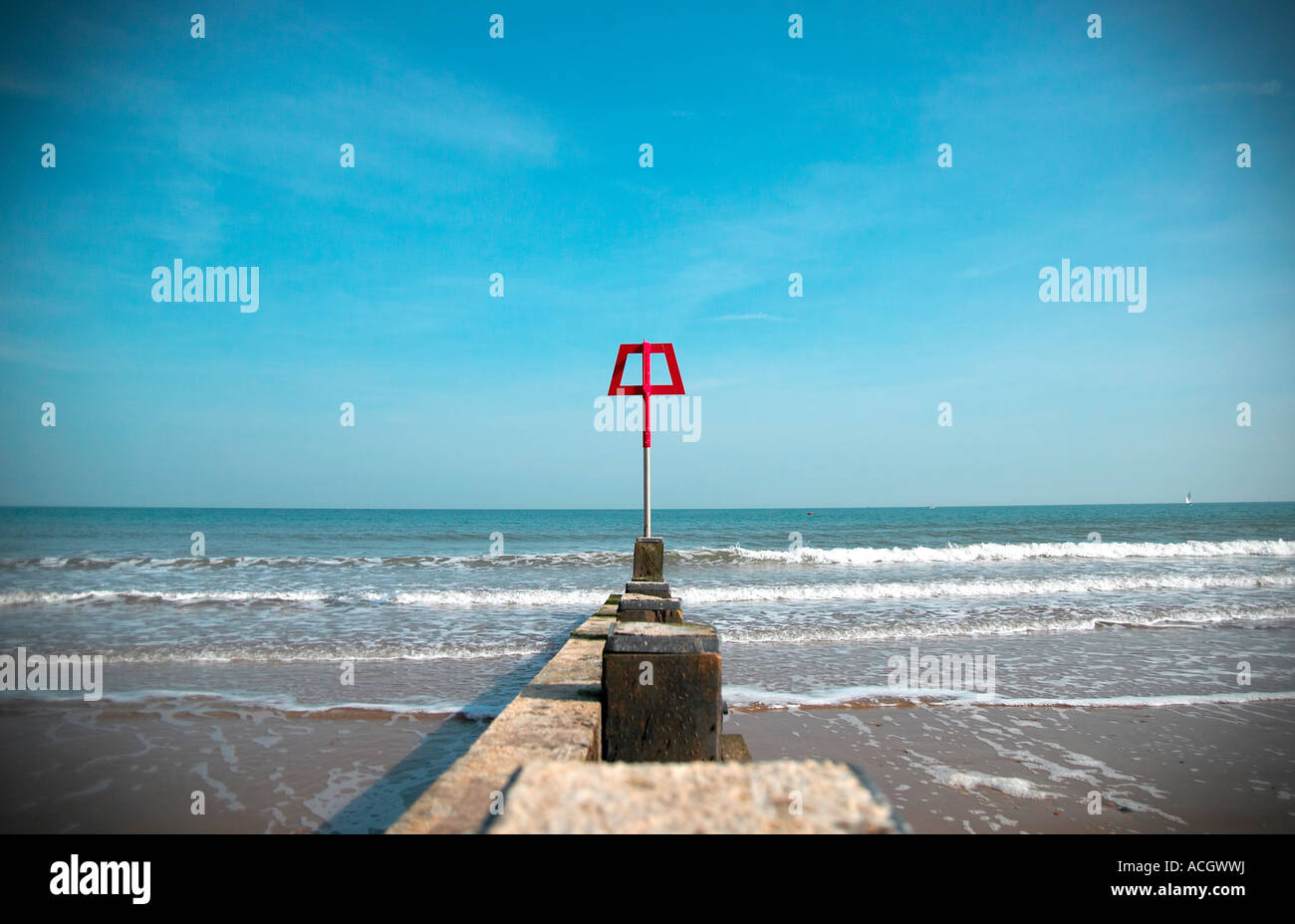 A bright red beach marker situated on a sea defence wall break. The ...
