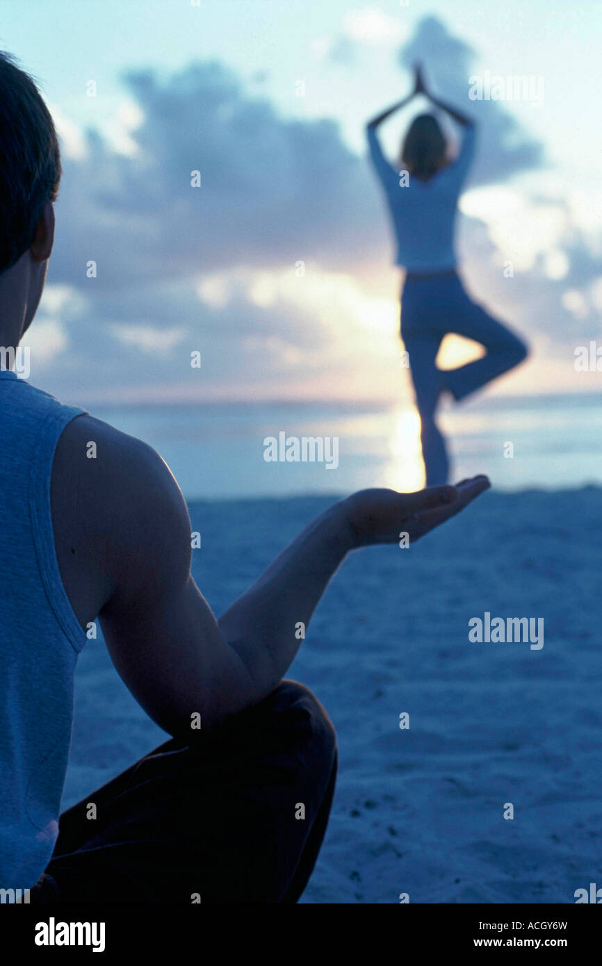 Couple doing exercise on ythe beach optical illusion Stock Photo - Alamy