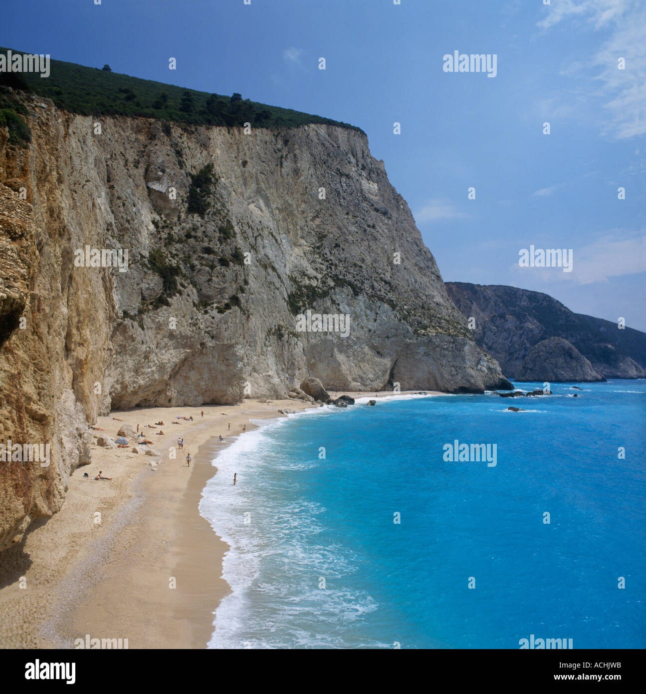 Rocky steep cliffs leading to blue sea with white waves and few people ...