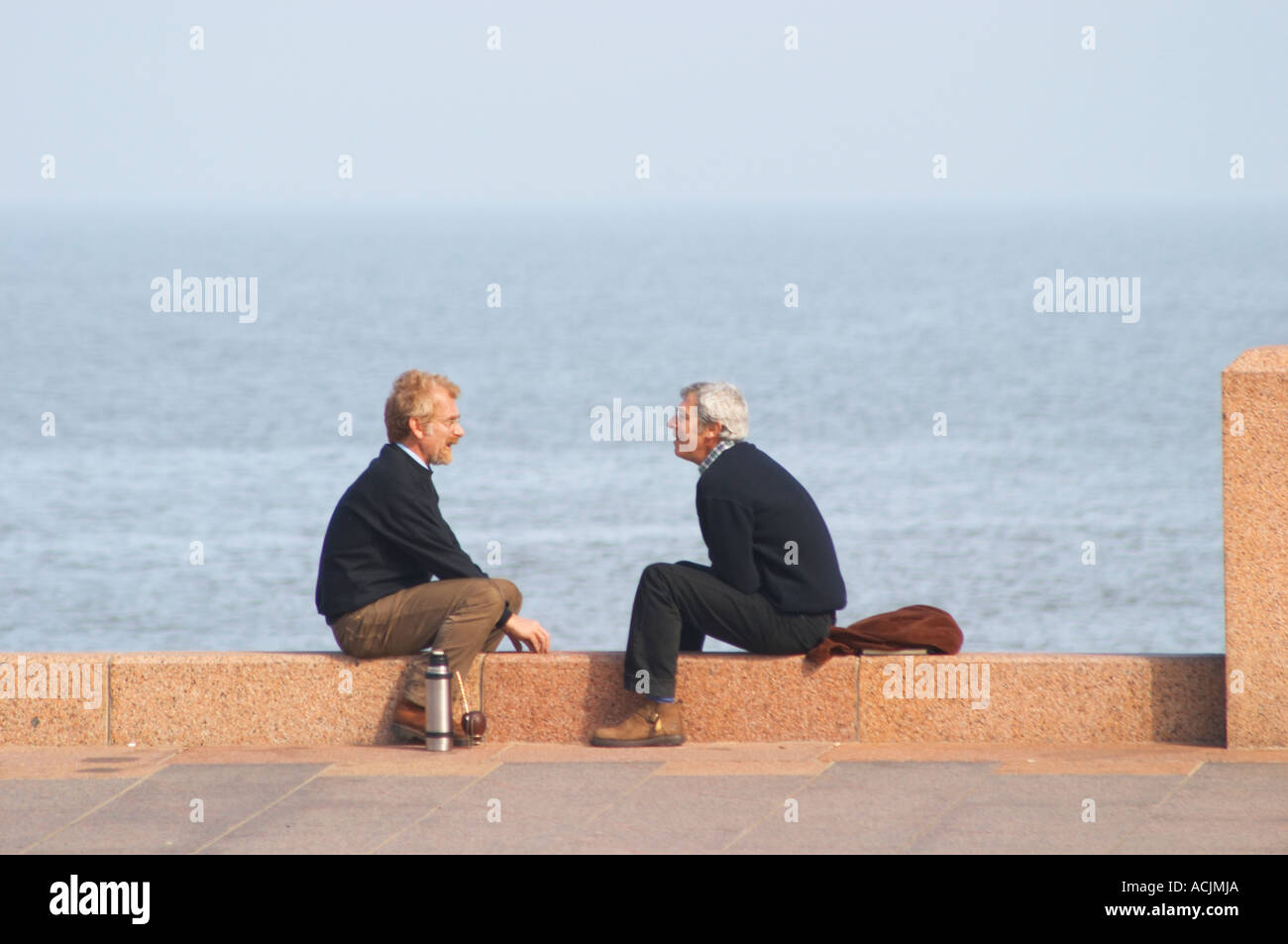 Two men sitting on a red stone bench. Men facing each other talking ...