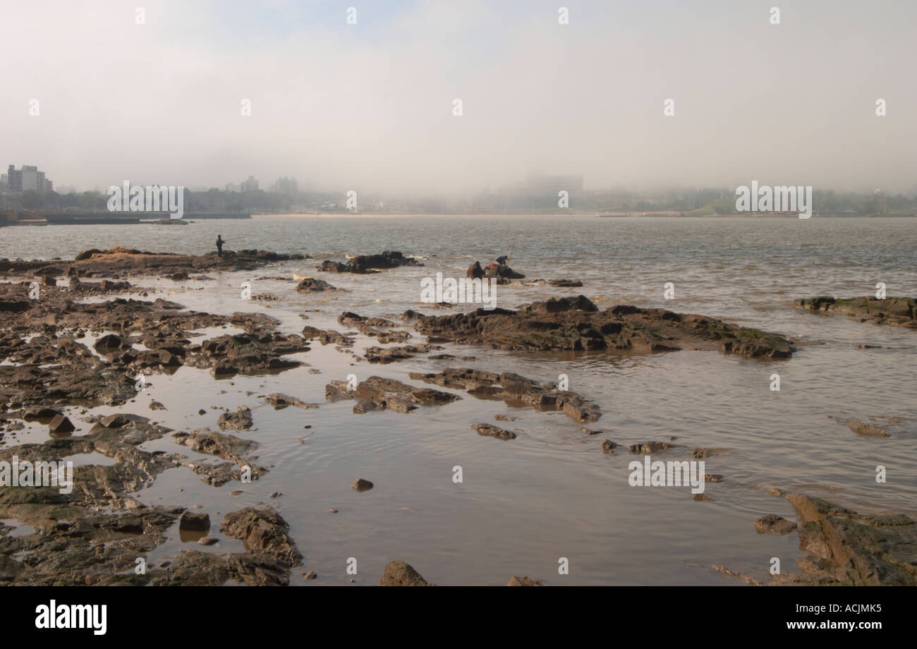 The city skyline in mist rocks in the foreground and men fishing from ...
