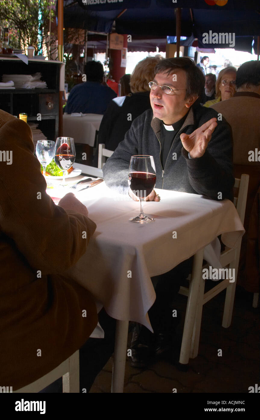 A priest in black and collar having lunch and a glass of wine and ...