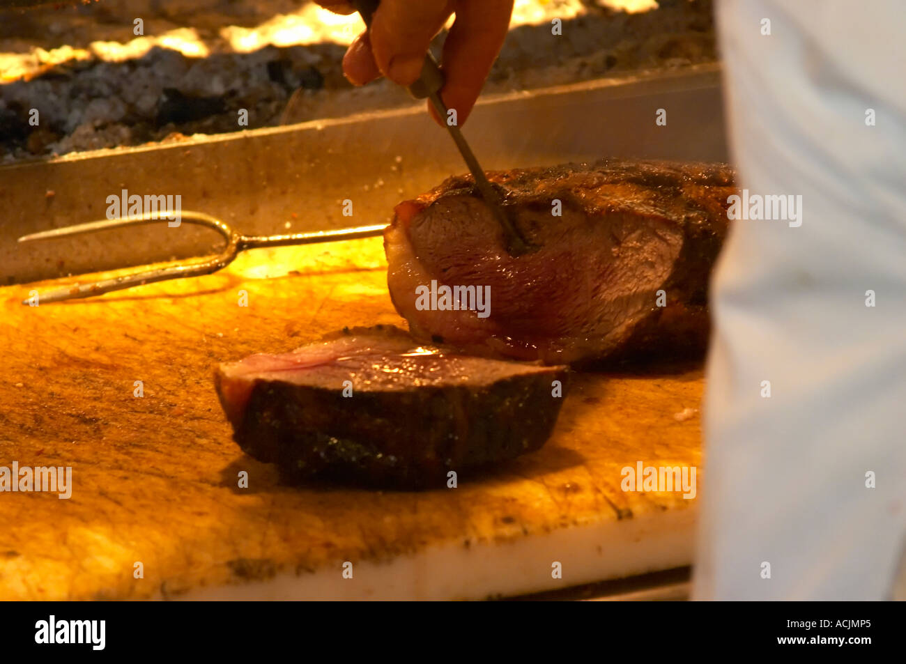 The chef cook carving cutting up a big piece of roast beef with a big ...