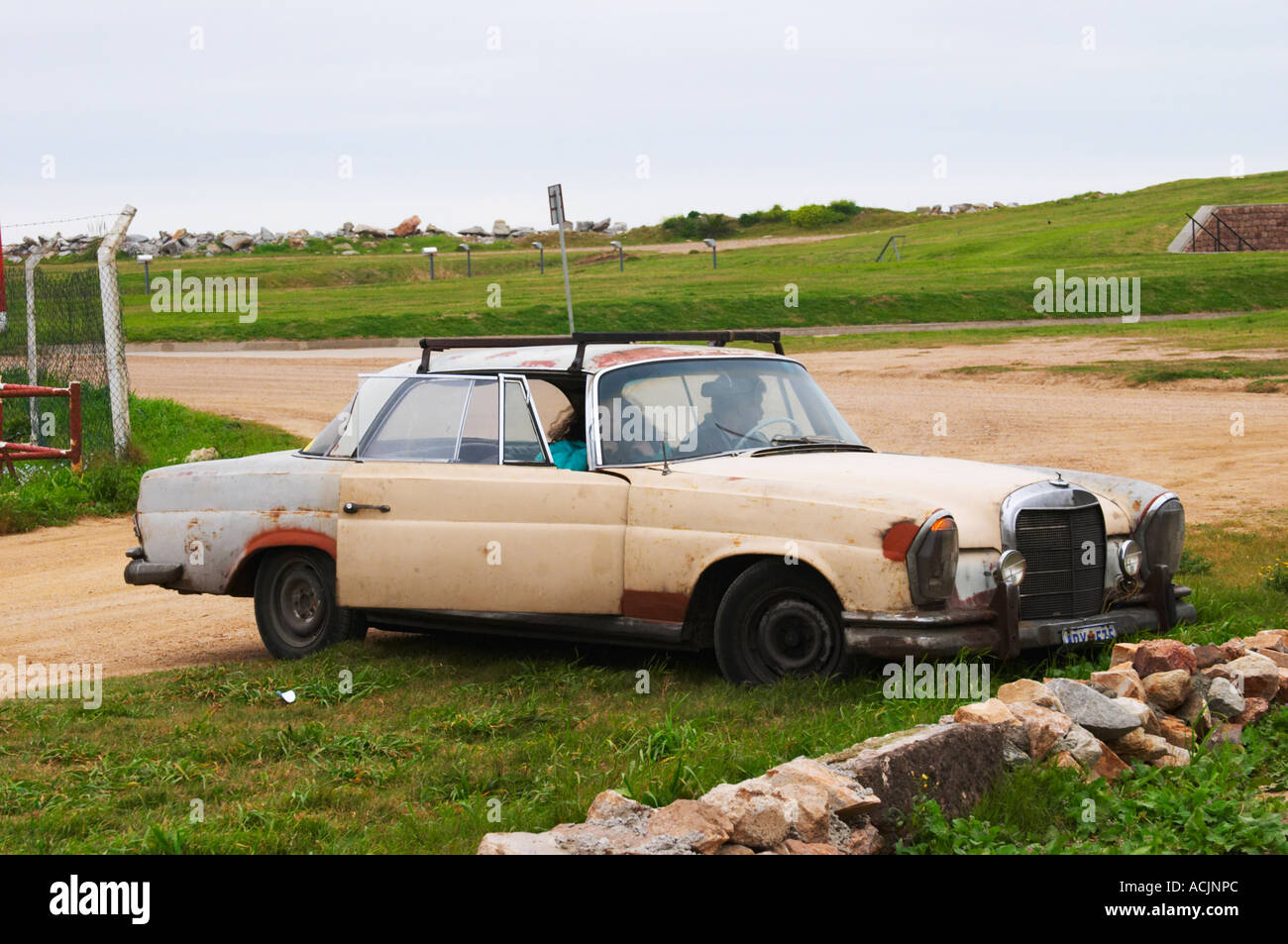 An old classic but run down and rusty Mercedes parked with two people ...