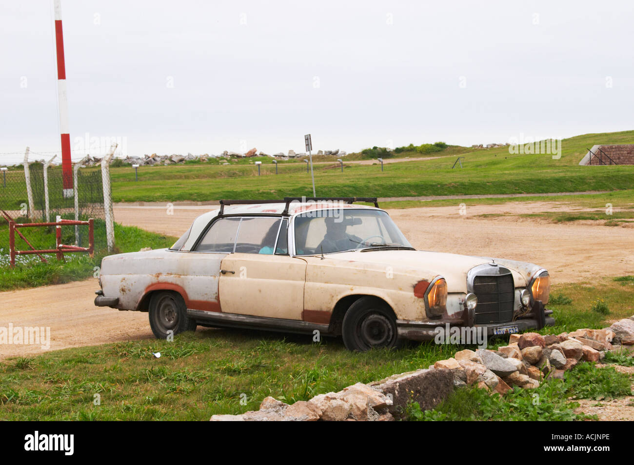 An old classic but run down and rusty Mercedes parked with two people ...