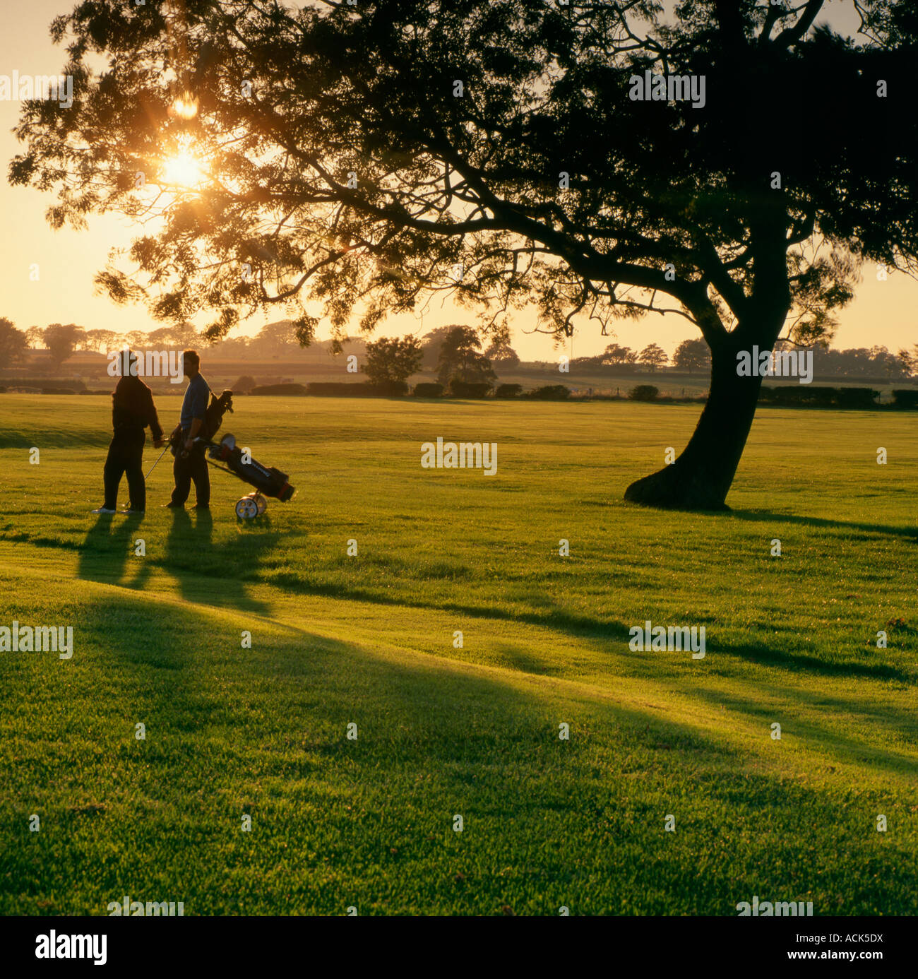 Two golfers walk onto the next hole in beautiful early morning sunshine ...