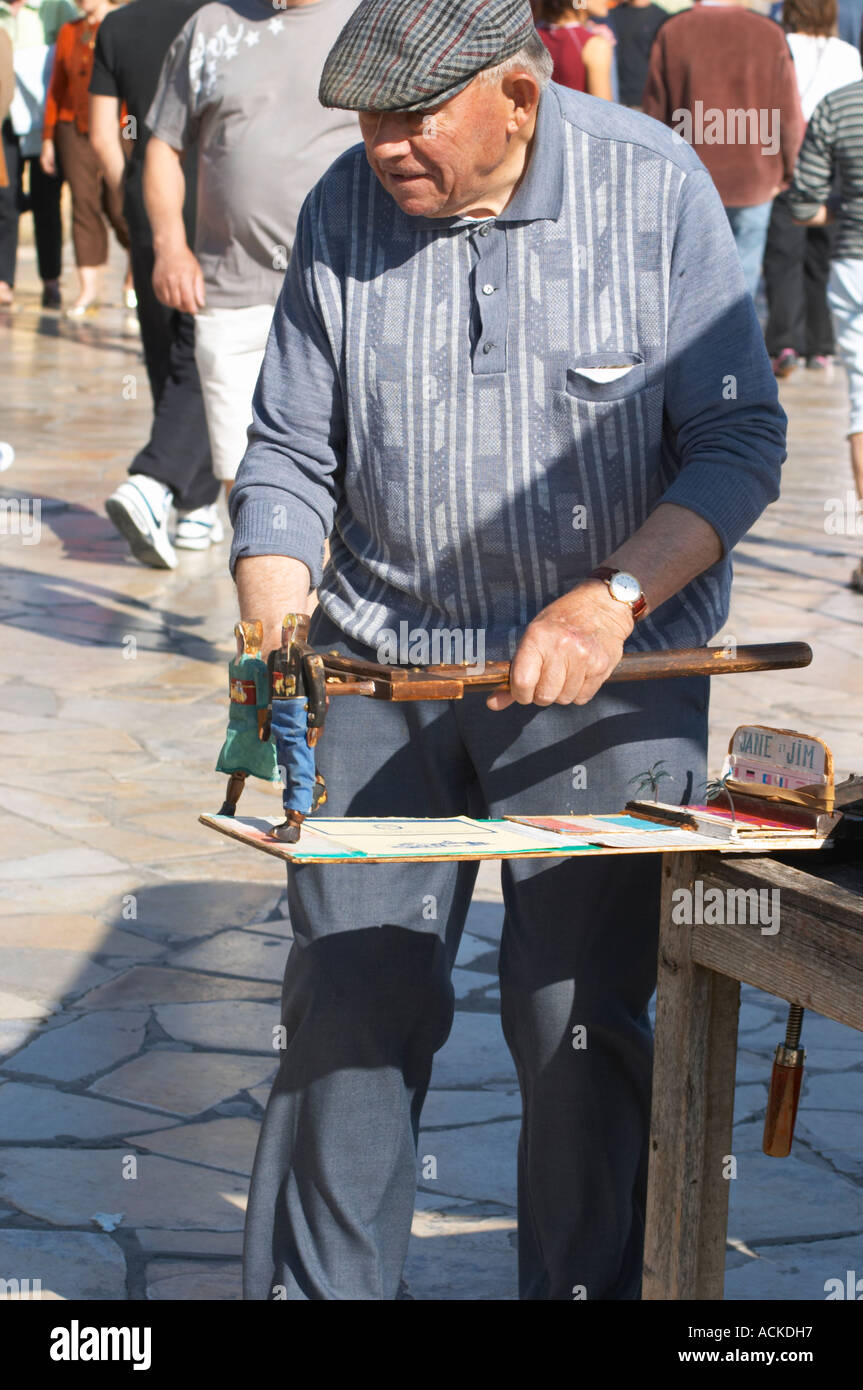A street entertainer, old man showing to children two carved wooden ...