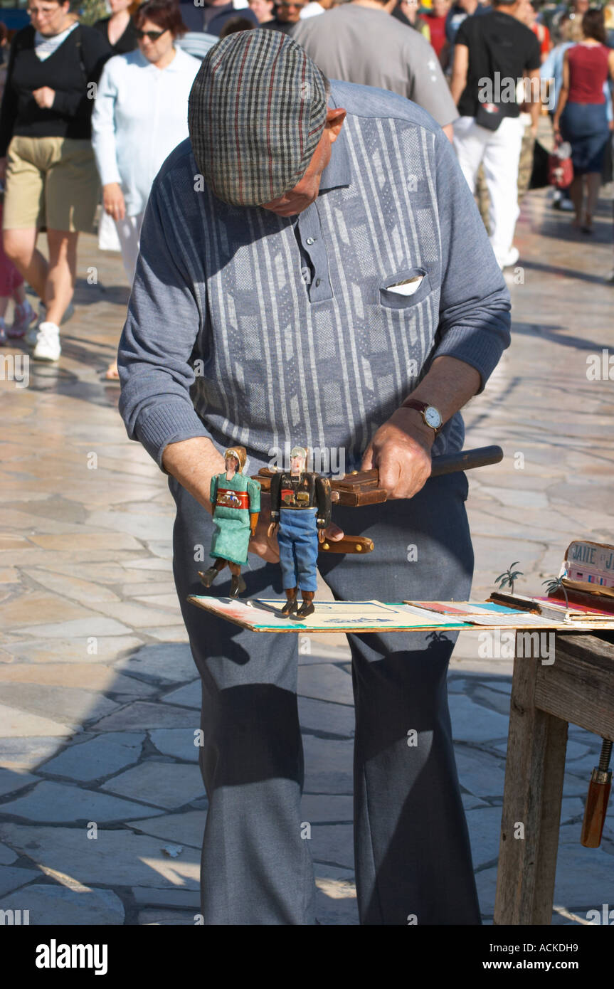 A street entertainer, old man showing to children two carved wooden ...