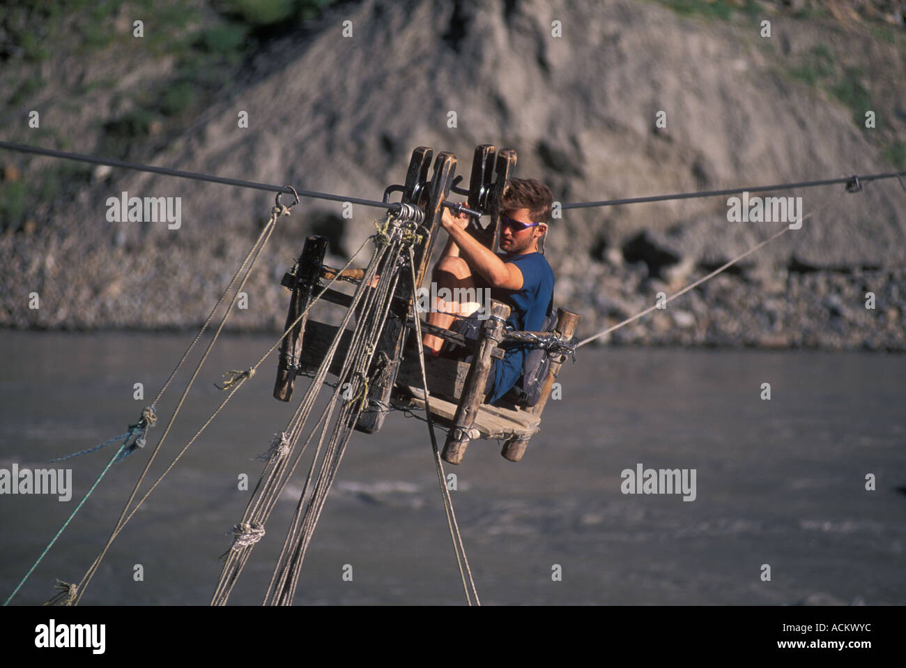 Adventurous traveler pulling himself across a cable rope bridge over a ...