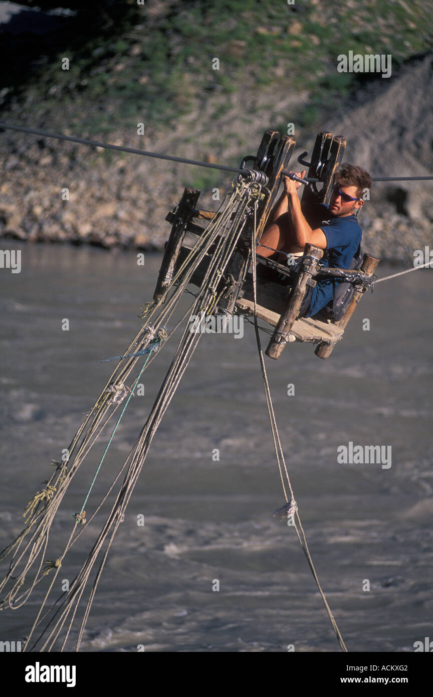 Adventurous traveler pulling himself across a cable rope bridge over a ...