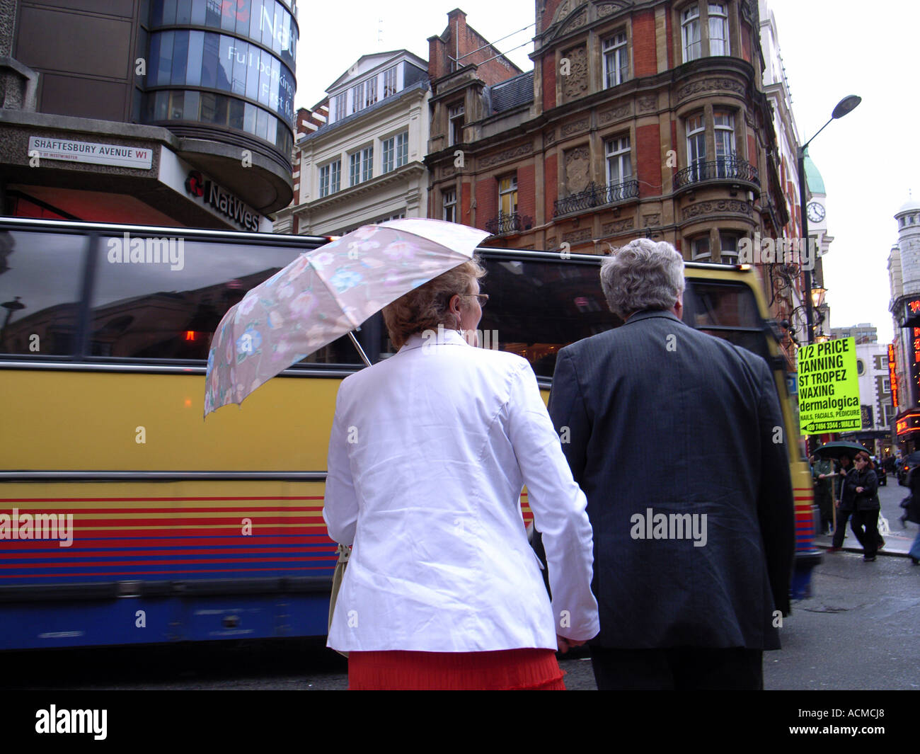 London UK street Scene couple with Umbrella in rain at corner of street ...