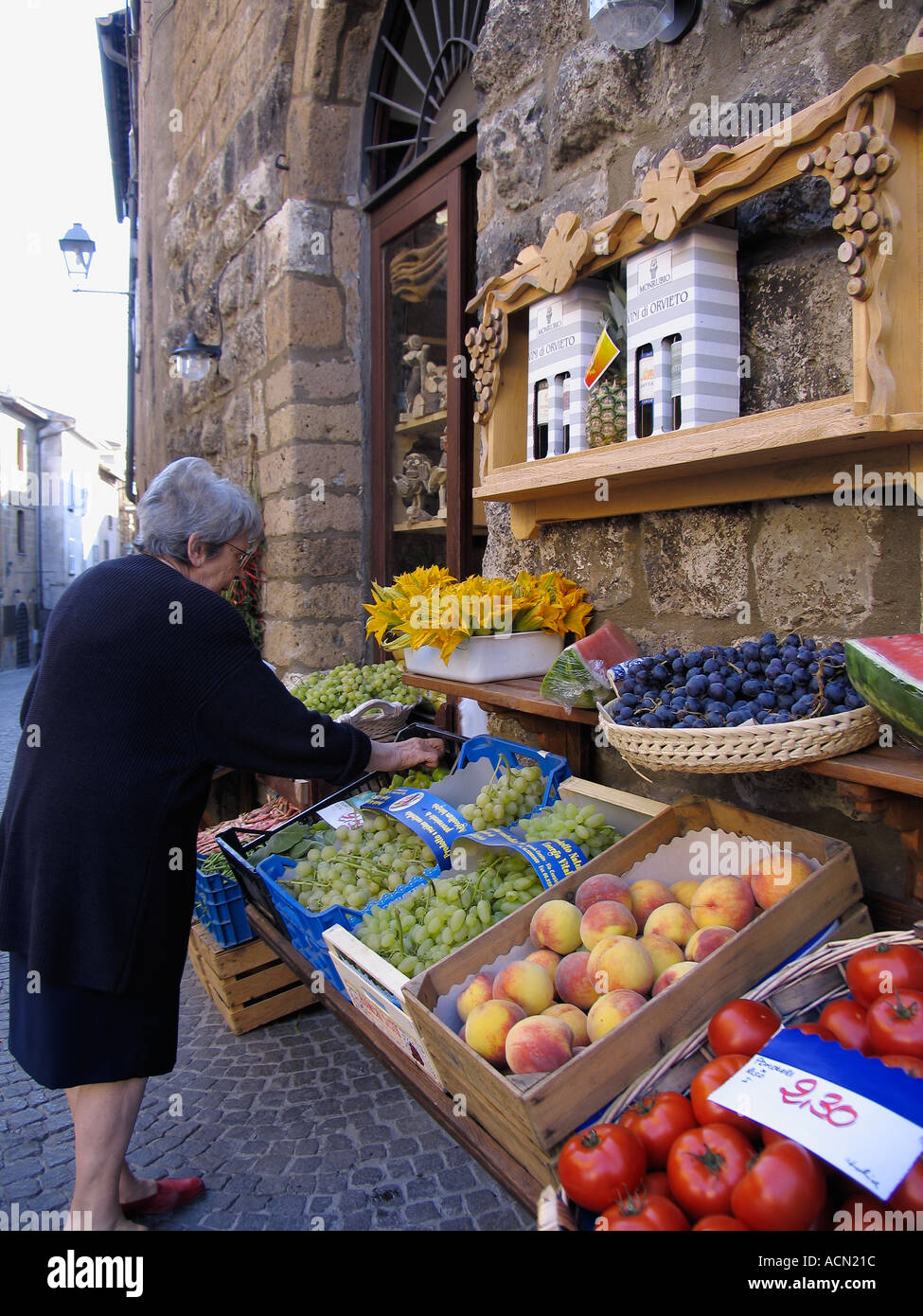 Woman picking out figs at fresh produce and fruit display outside shop ...