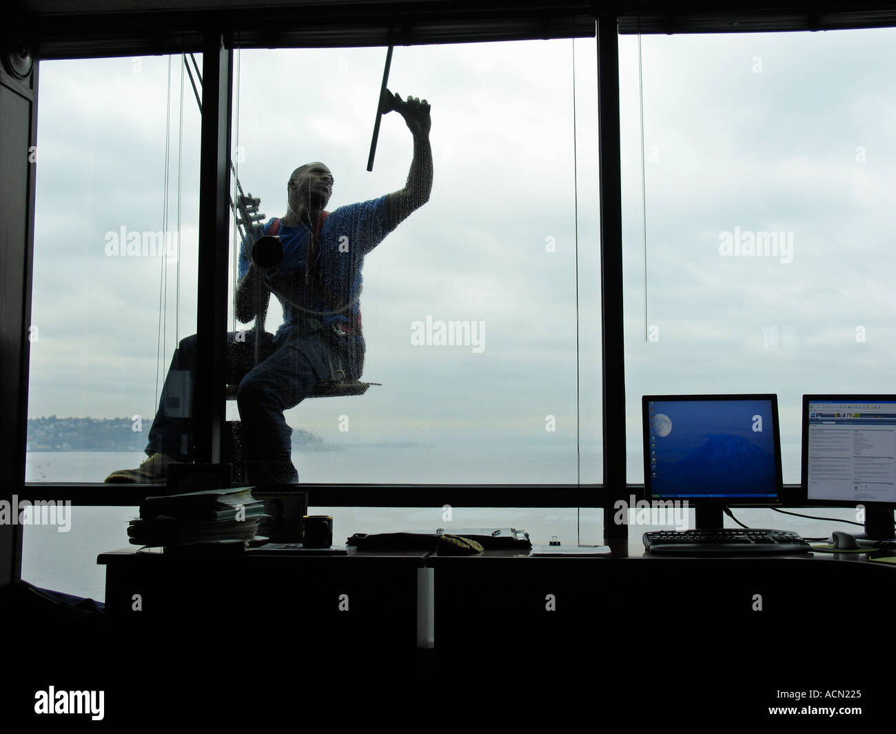 Man suspended on bosun chair washing plate glass window in highrise ...