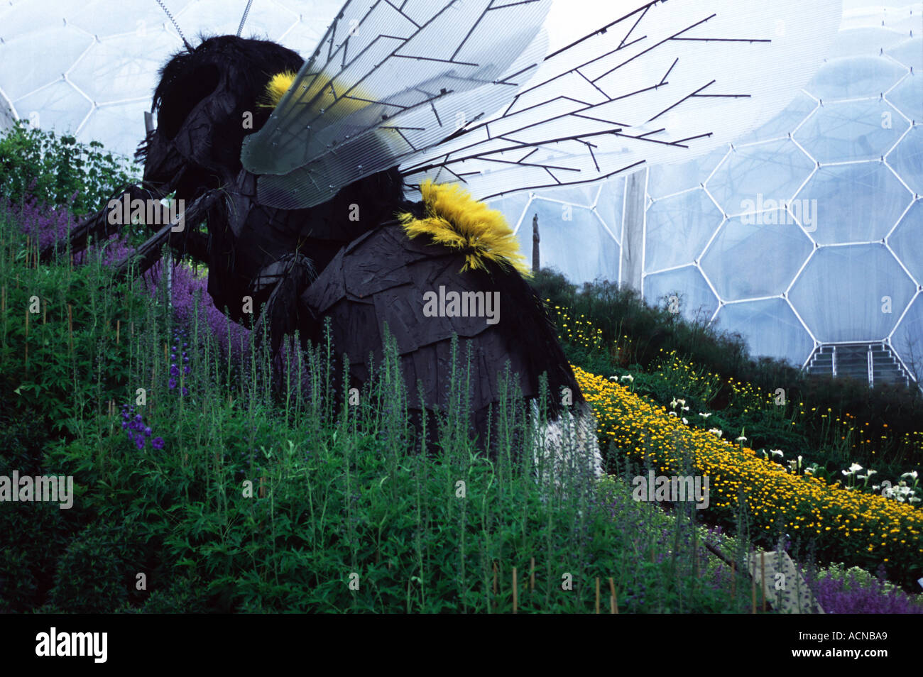 A large bee statue or sculpture nestles in the flowers with a Biod-ome ...