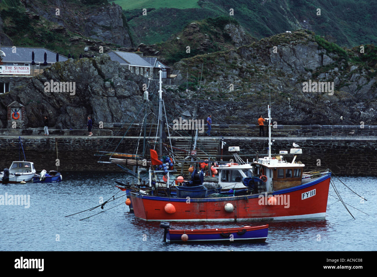 Dramatic rocky backdrop to some red trawlers in the harbour typical of ...