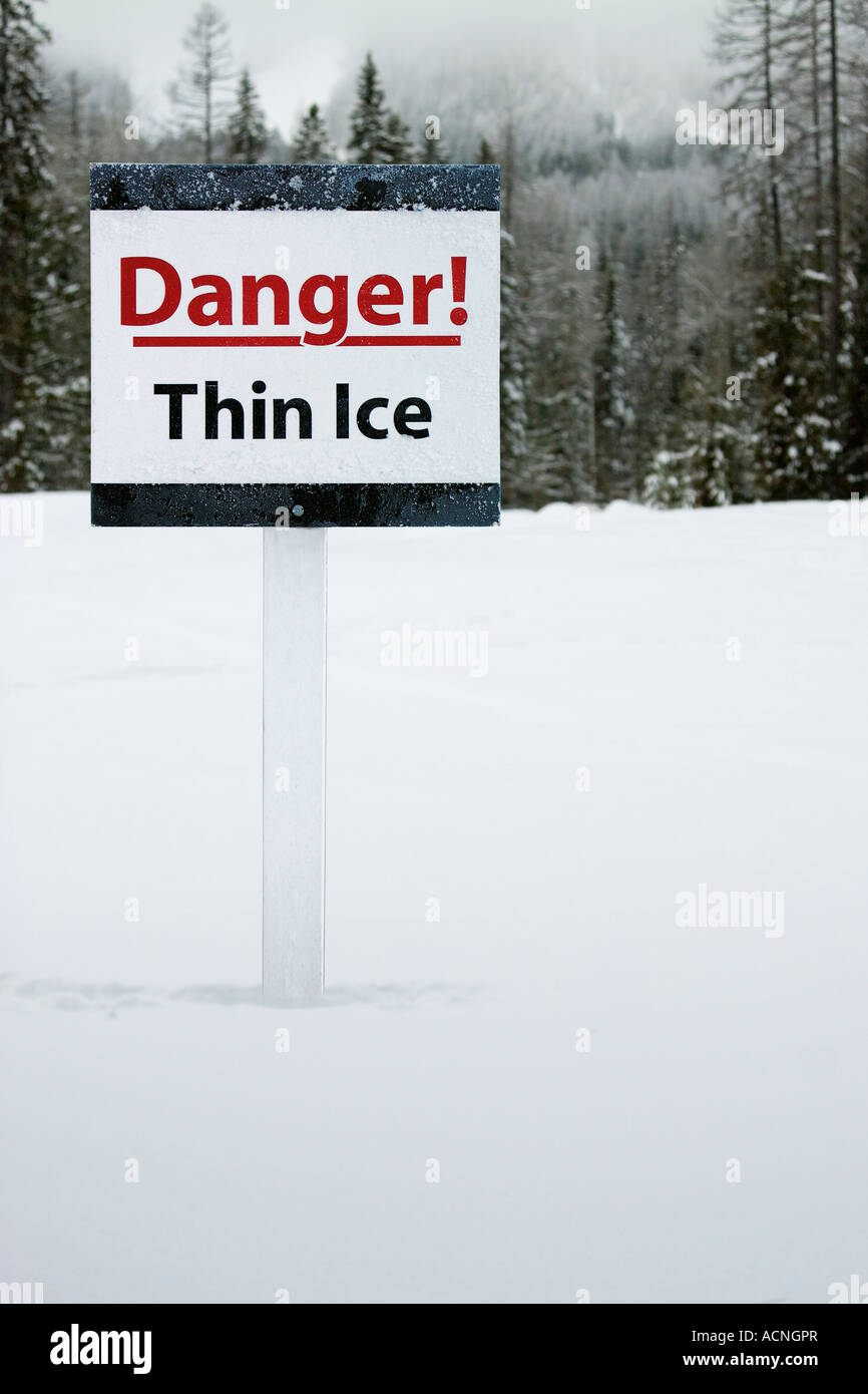 Danger! Thin Ice frost-covered sign at edge of frozen body of water ...