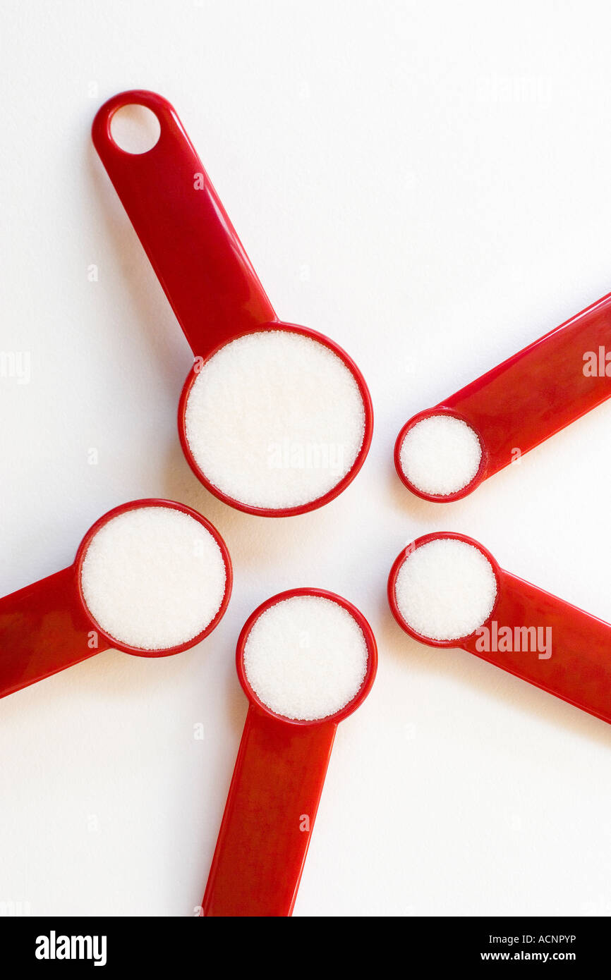 Five red measuring spoons filled with salt arranged in a circle on a ...