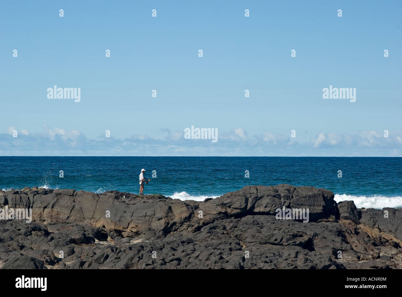 a single person standing and fishing on the rocks Stock Photo - Alamy