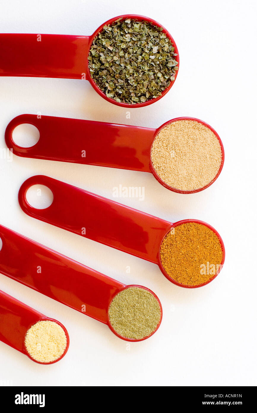 Five red measuring spoons filled with spices arranged in descending ...