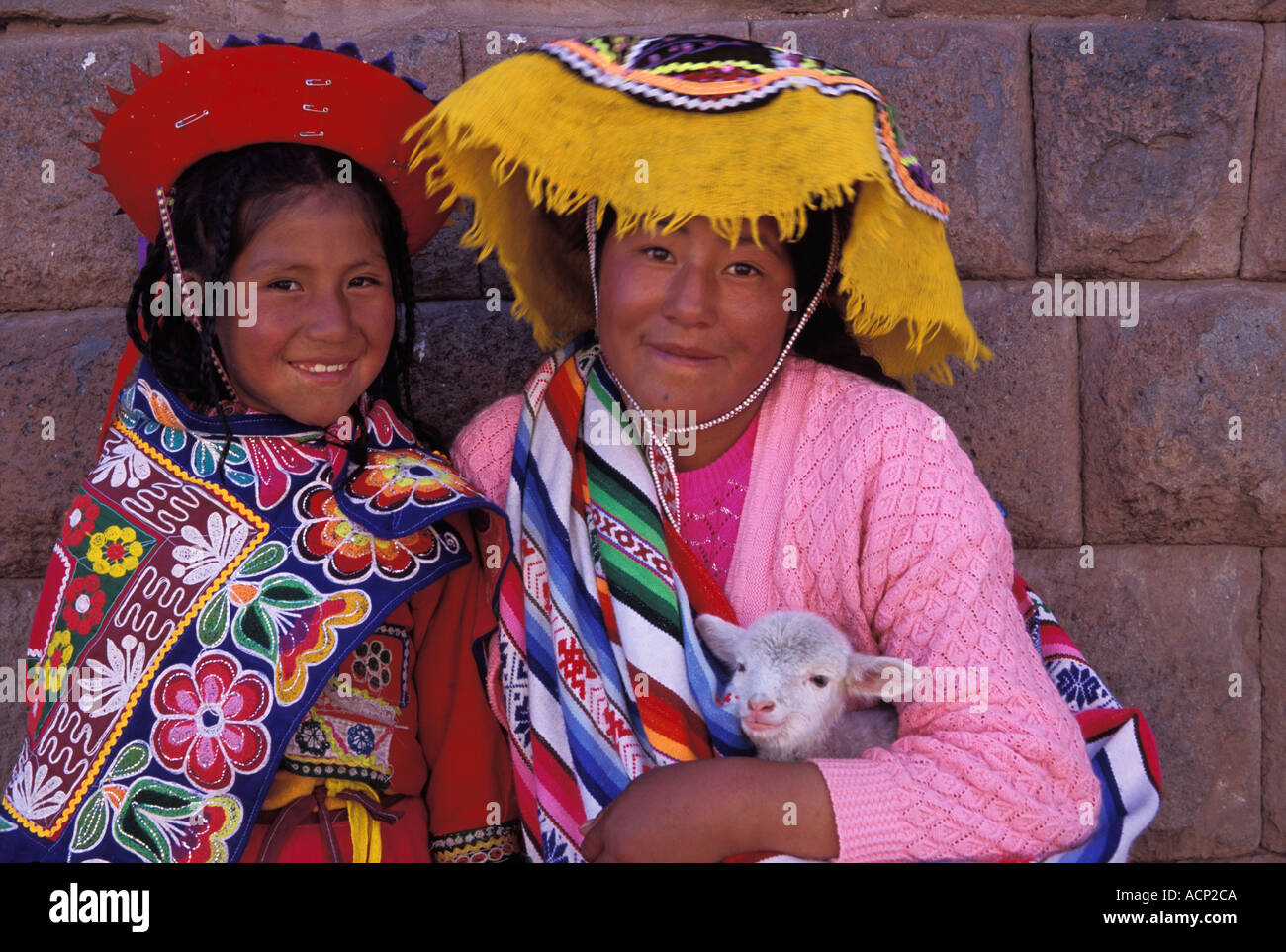 Two Indian girls holding a lamb in front of ancient Inca stone wall ...