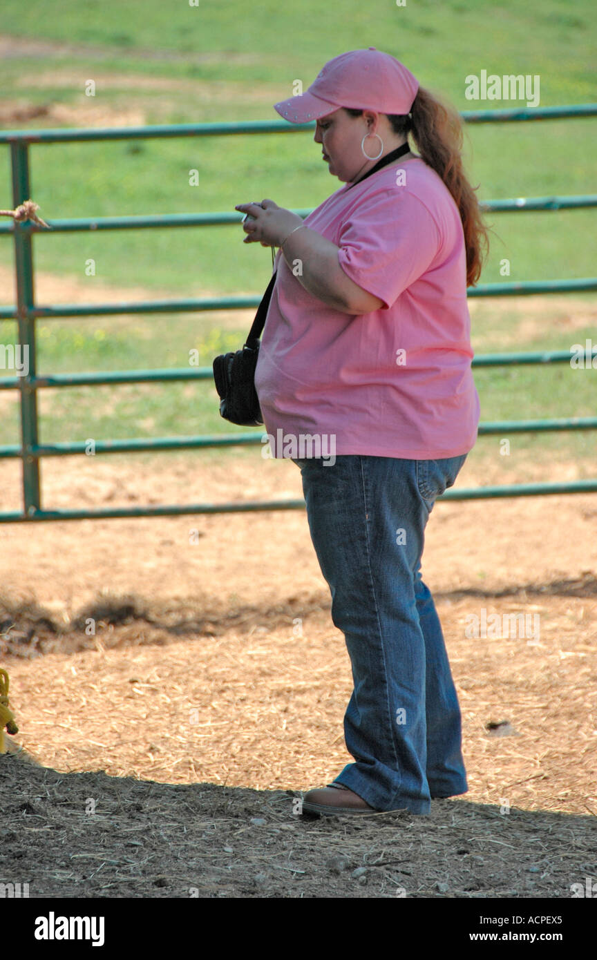 Very large woman on fence at dude ranch in the country watching cattle ...
