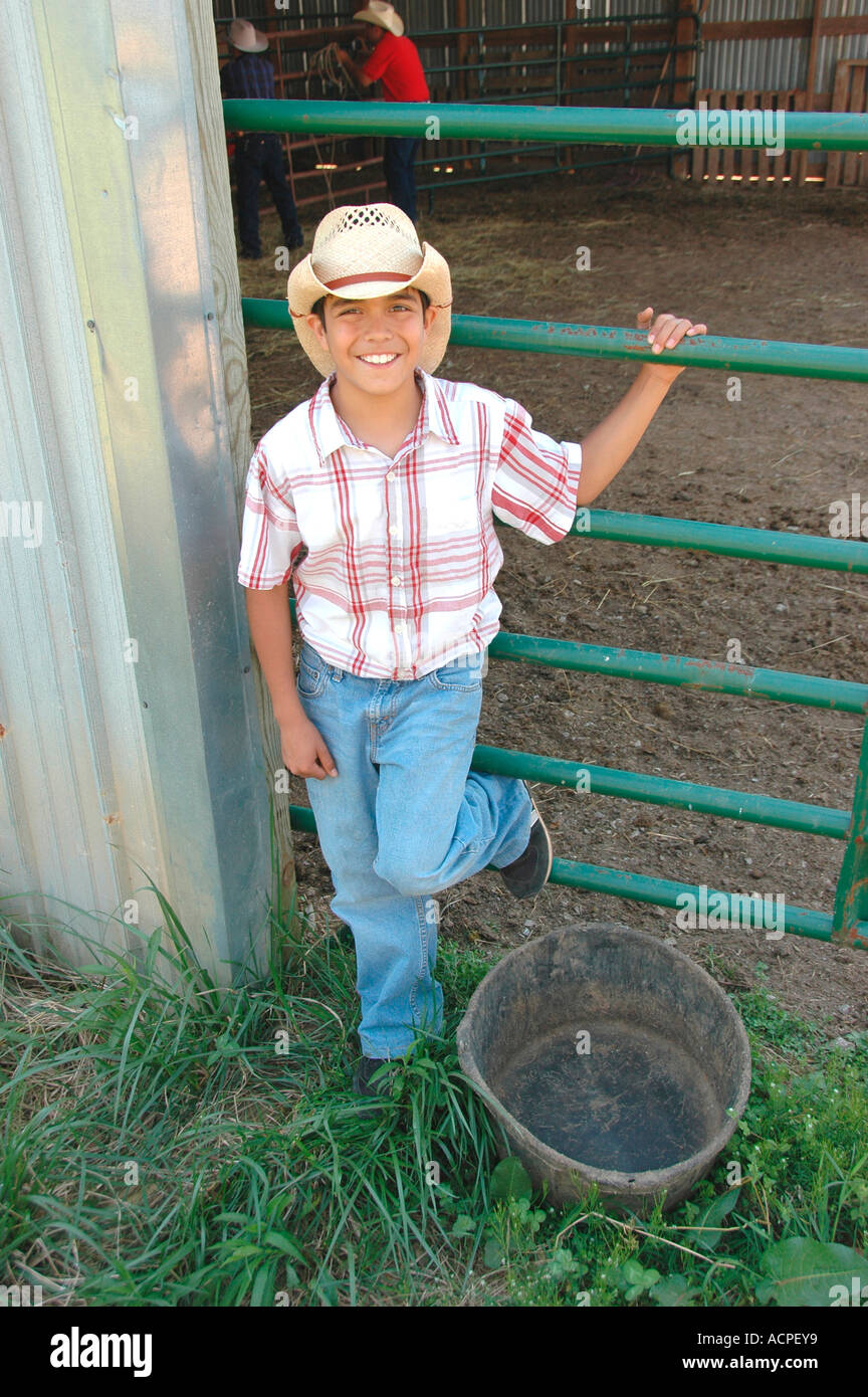 Very young ranch hand son of cowboy at barn fence during roundup with ...