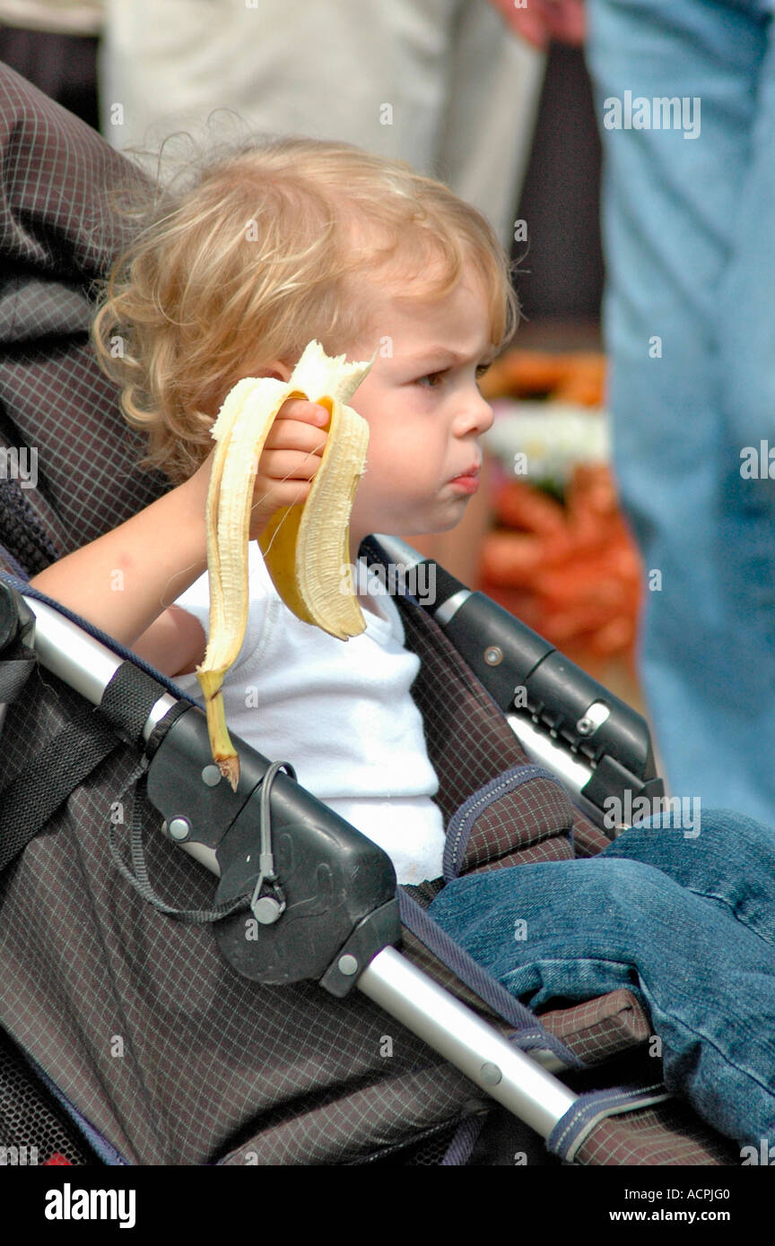 Blond toddler Baby boy eating banana while sitting in stroller Stock ...
