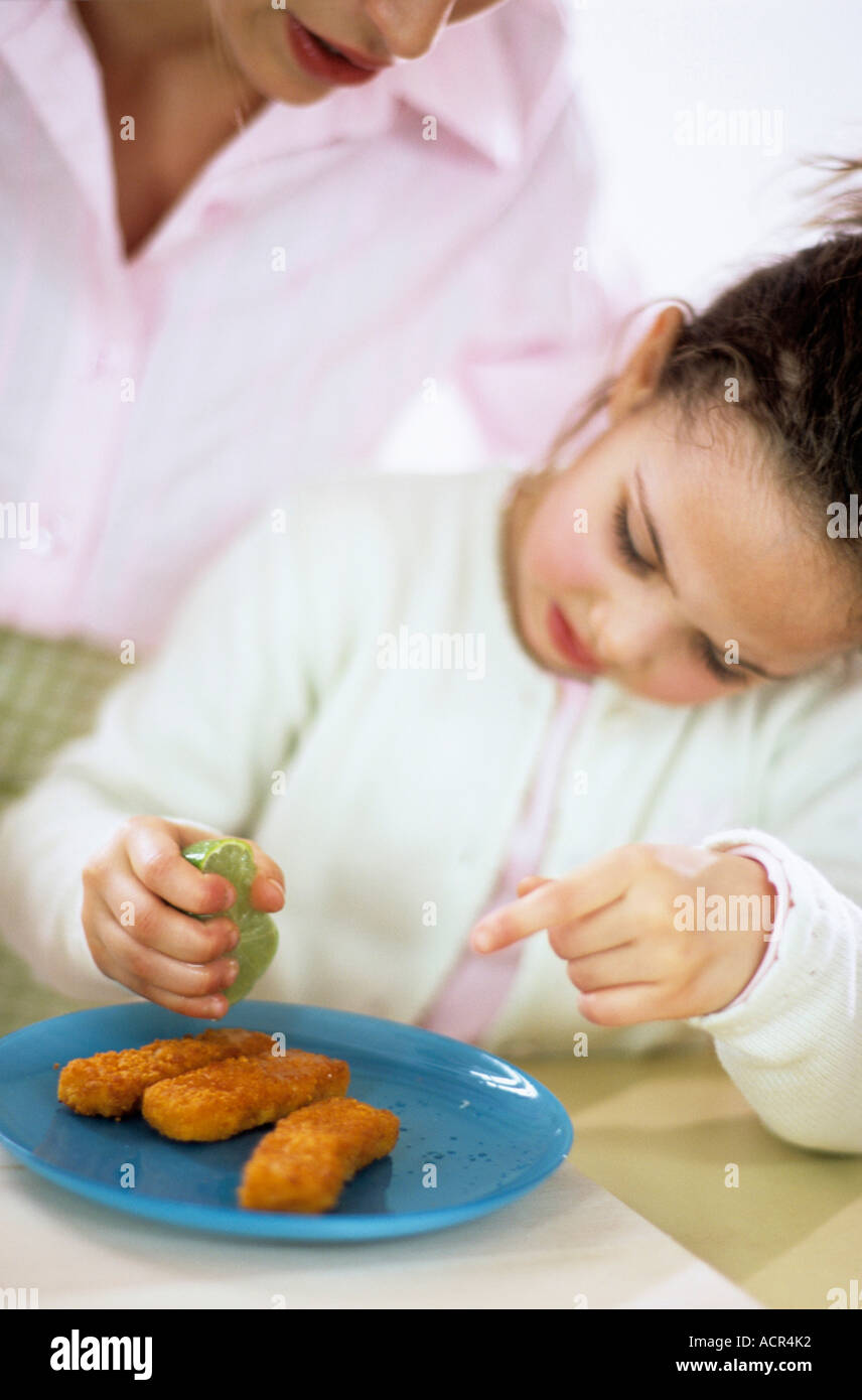Girl squeezing lemon over fish sticks Stock Photo - Alamy