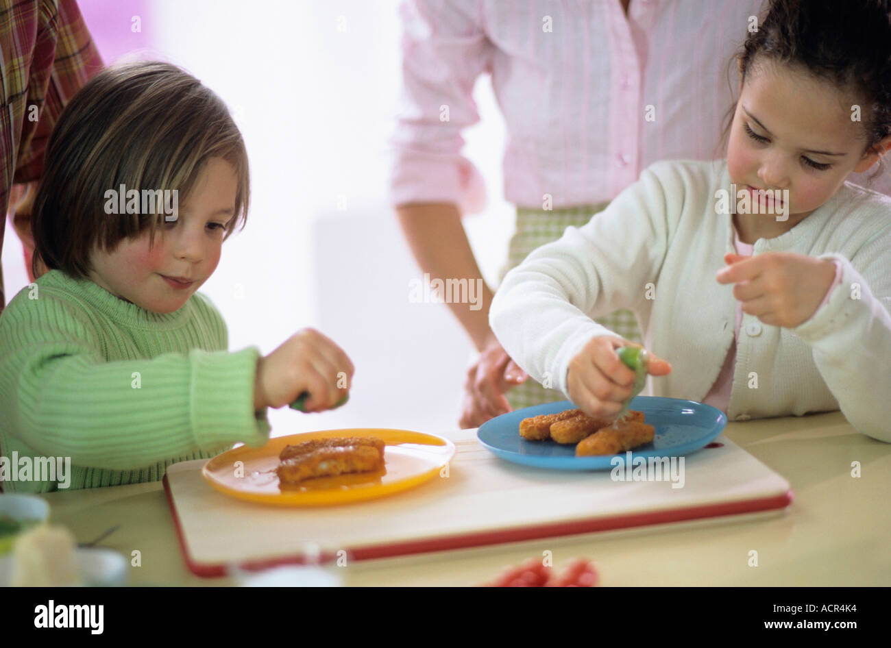 Children squeezing lemon over fish sticks Stock Photo - Alamy