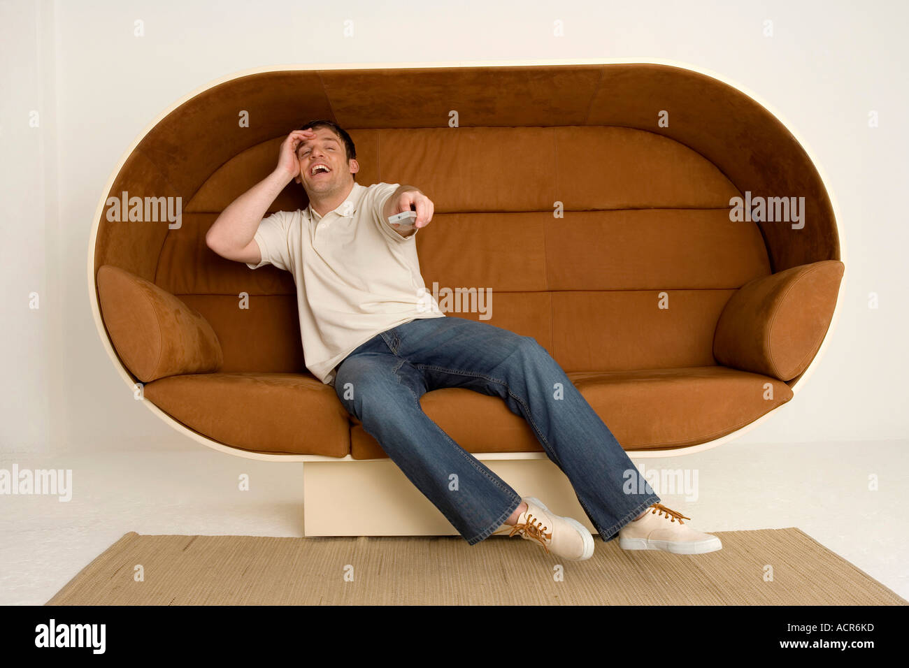 Young man sitting on sofa, holding remote control Stock Photo - Alamy