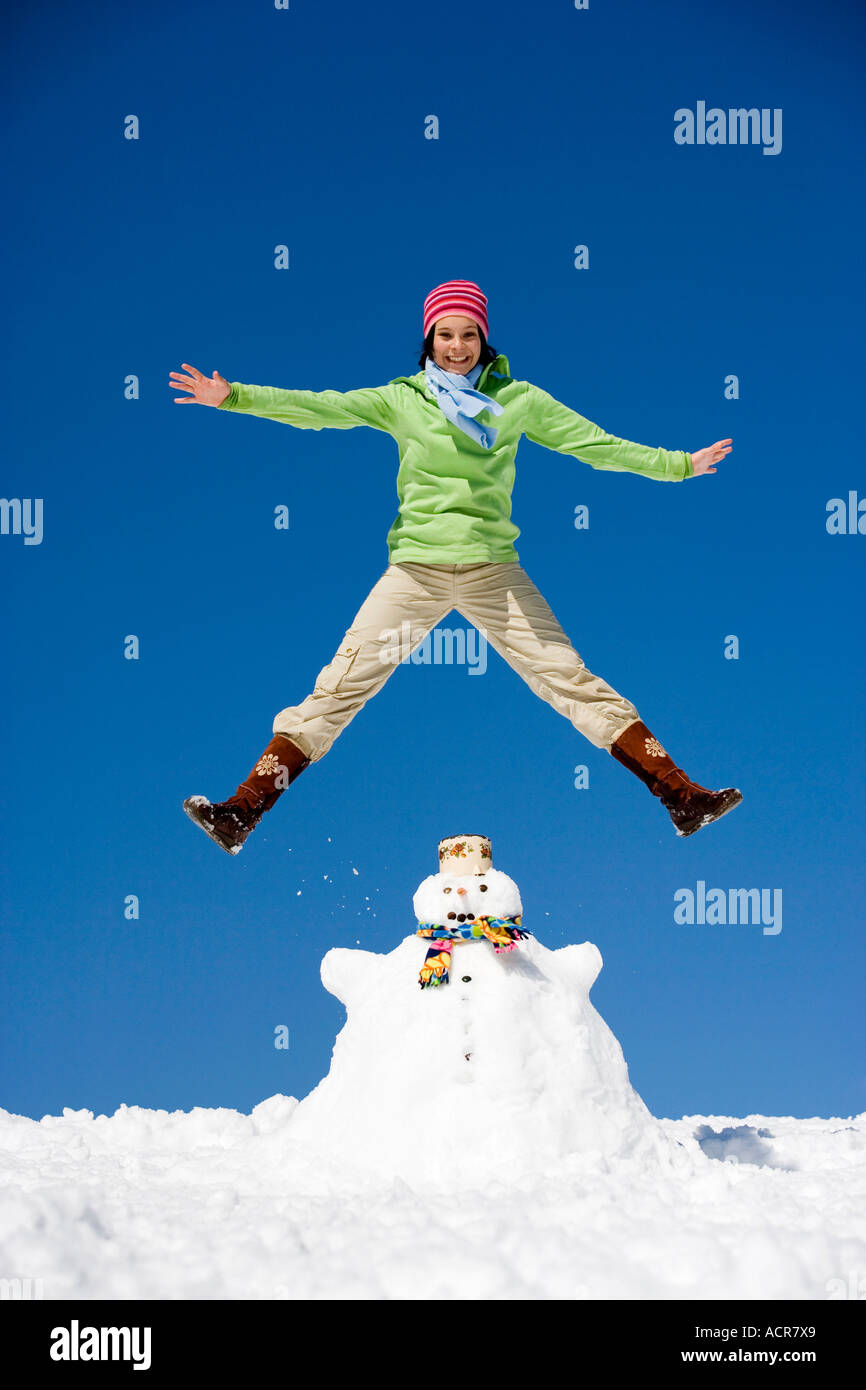 Austria, teenage girl (16-17) jumping on snowman, smiling, low angle ...