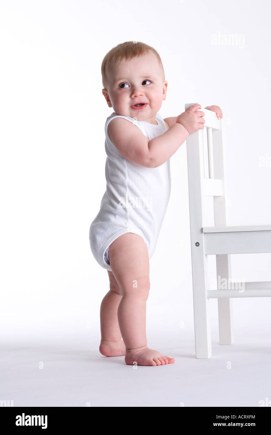 Baby boy standing against a little chair Stock Photo - Alamy
