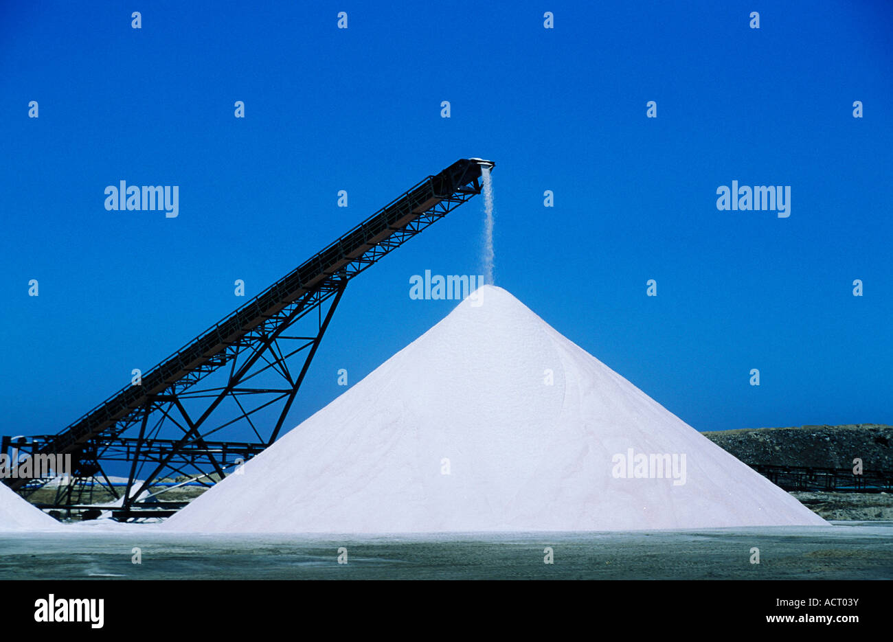 View of raw salt being poured onto a stockpile by a conveyer belt ...