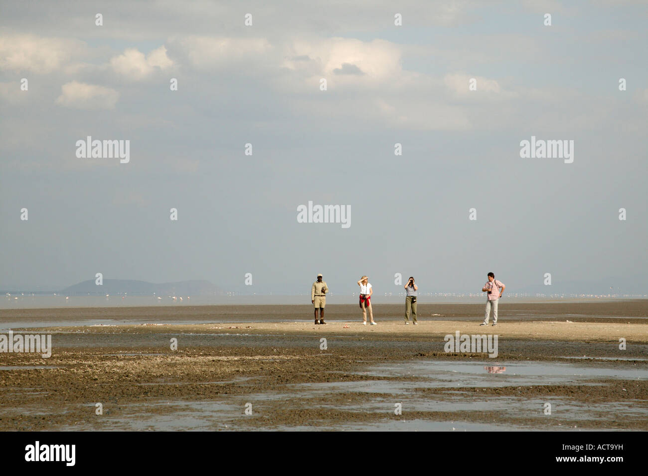 Three tourists and their guide stand on the plains adjacent to Lake ...