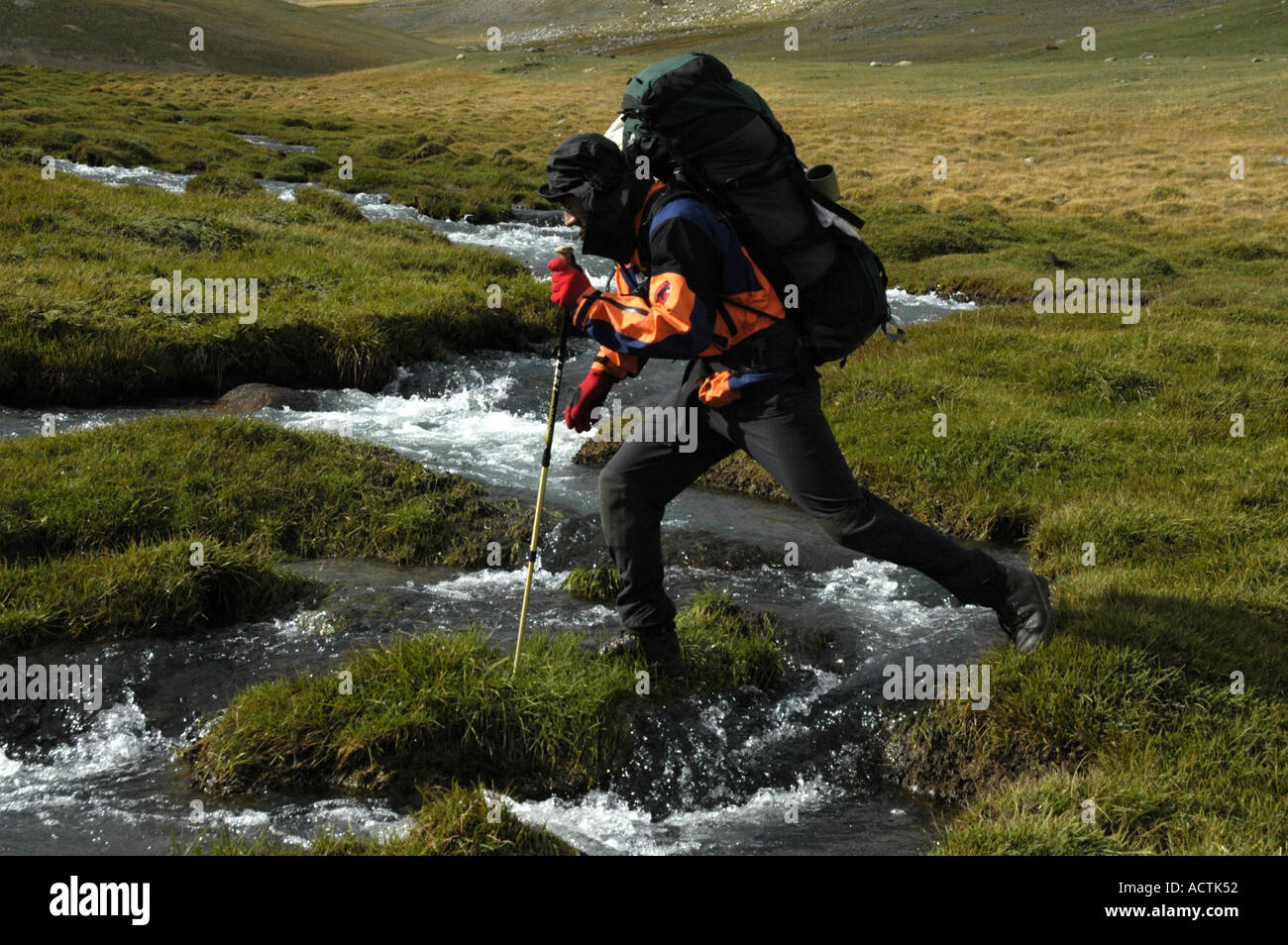 MR Mountaineer carrying a backpack jumps over a creek in the steppe ...