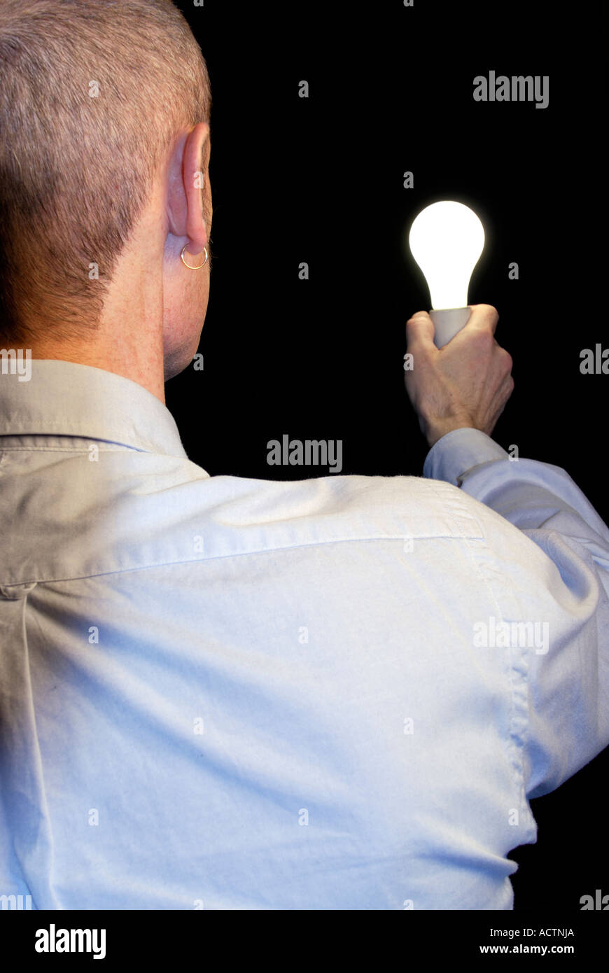Back of man holding up a lit light bulb illuminating the dark Stock ...