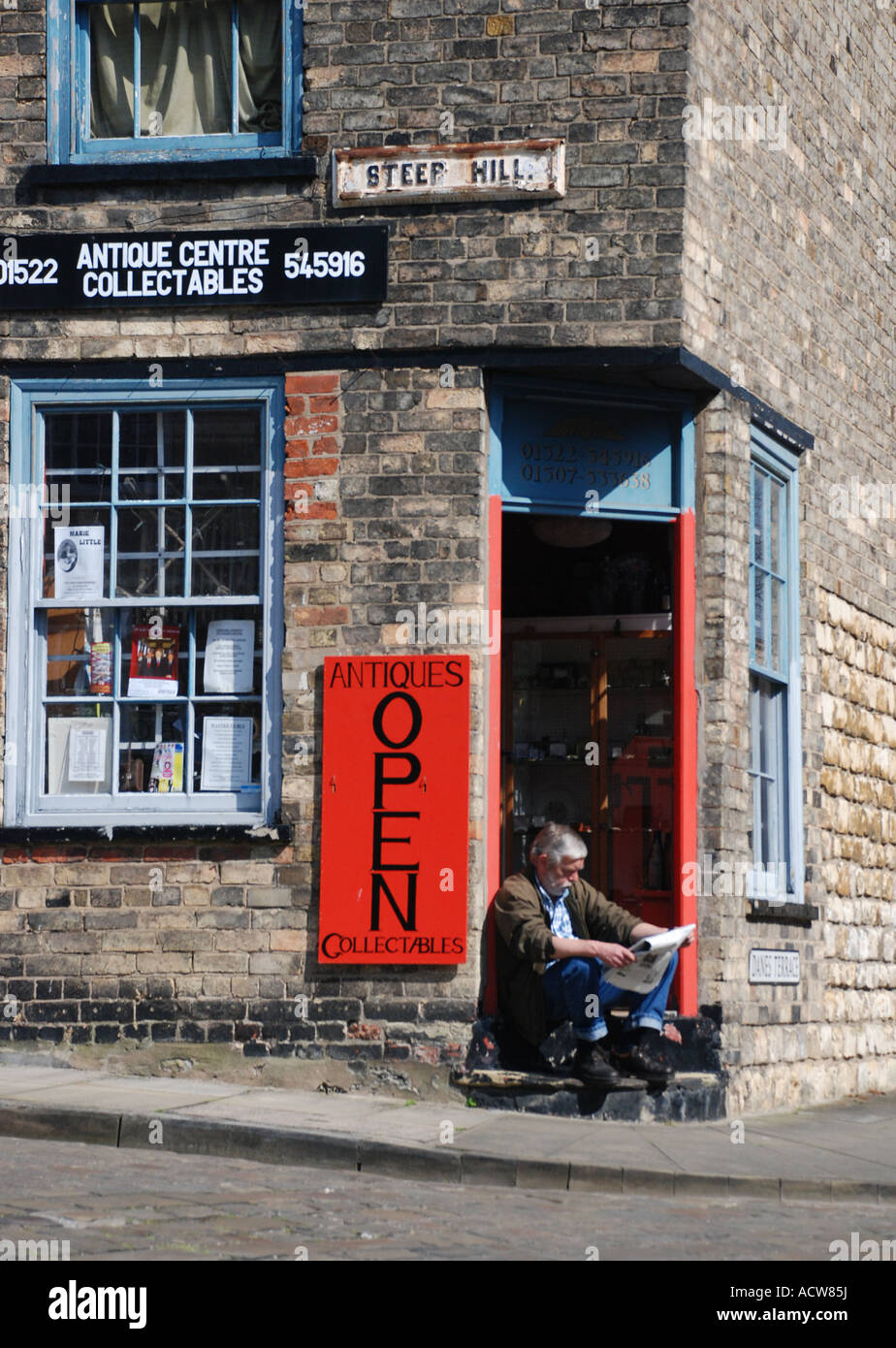 Antique sat reading newspaper outside Antique shop Stock Photo - Alamy
