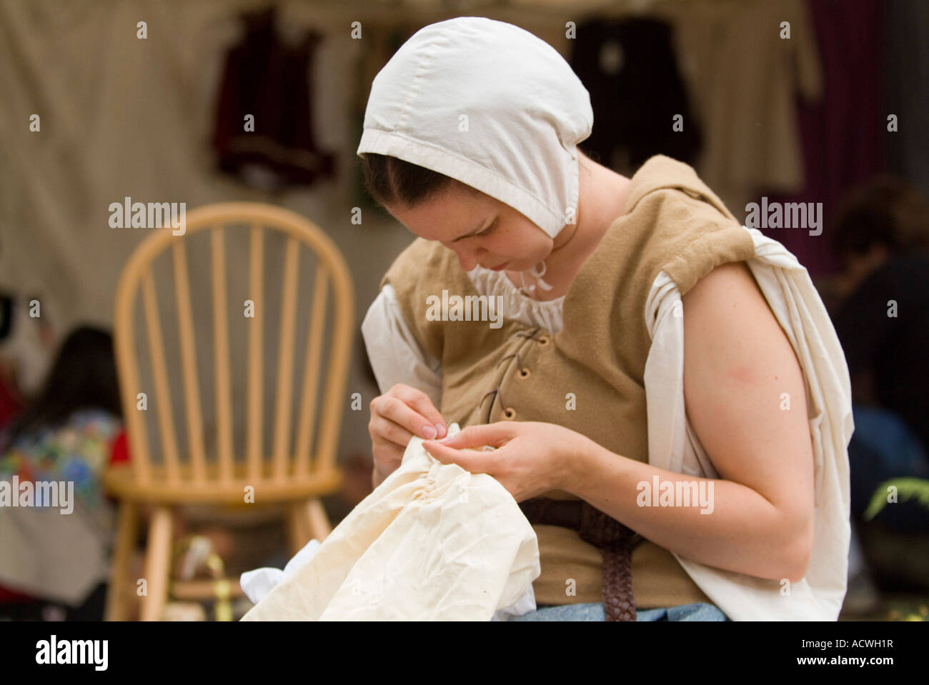 A WOMAN DRESSED IN MEDIEVAL CLOTHES IS DOING NEEDLE WORK ON CLOTHES ...
