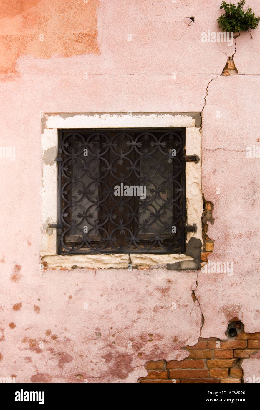grated window in a brick wall covered with chipped and peeling stucco ...