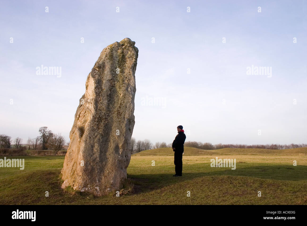 Man standing beside tall single stone at Avebury Stone Circle in ...