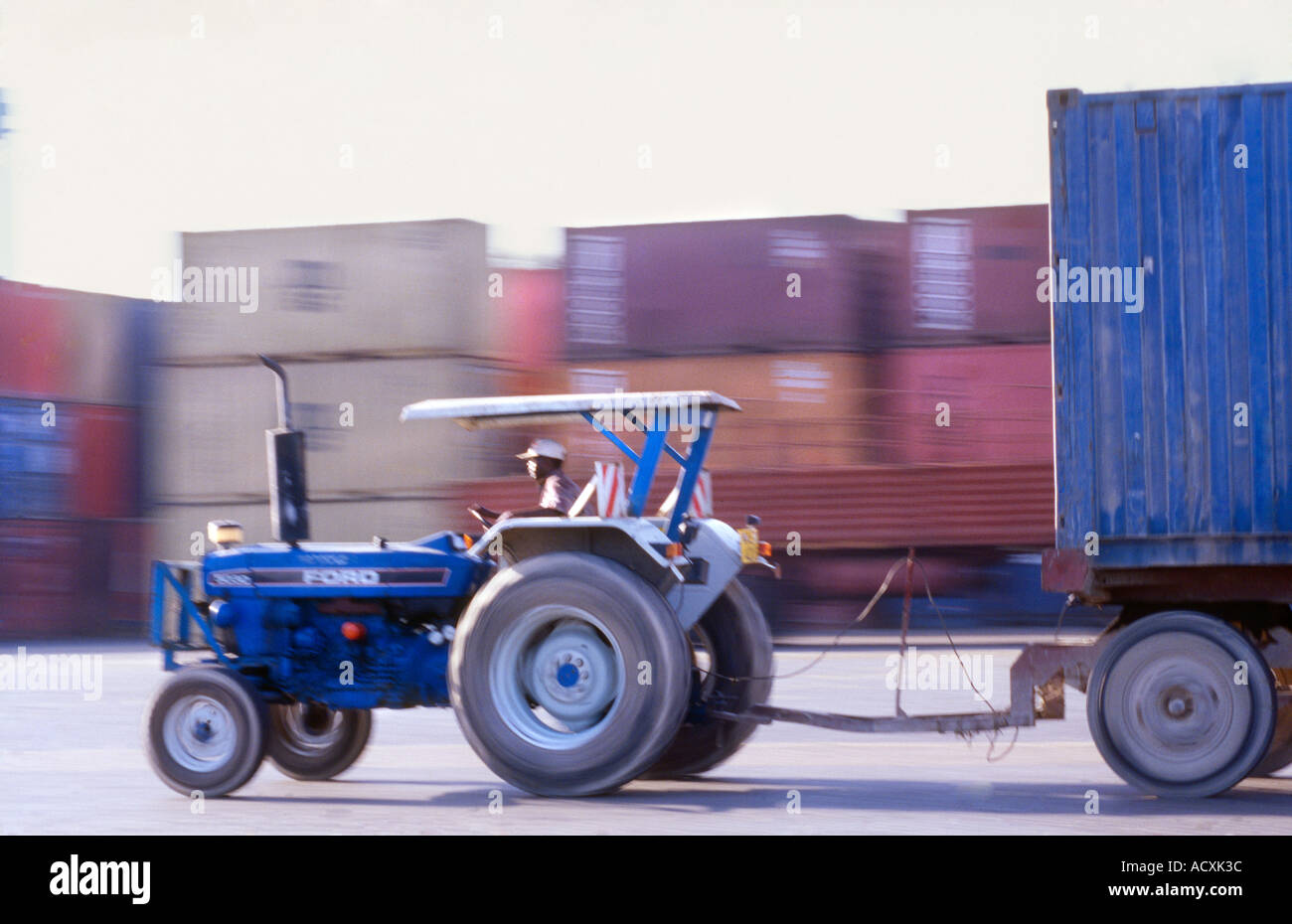 blurred photo of man driving a tractor pulling a ship container to load ...