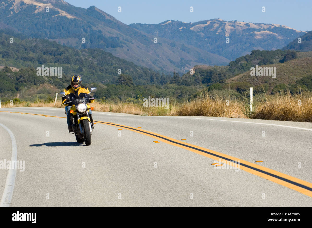 Single mature female motorcyclist rides motorcycle along pacific coast ...