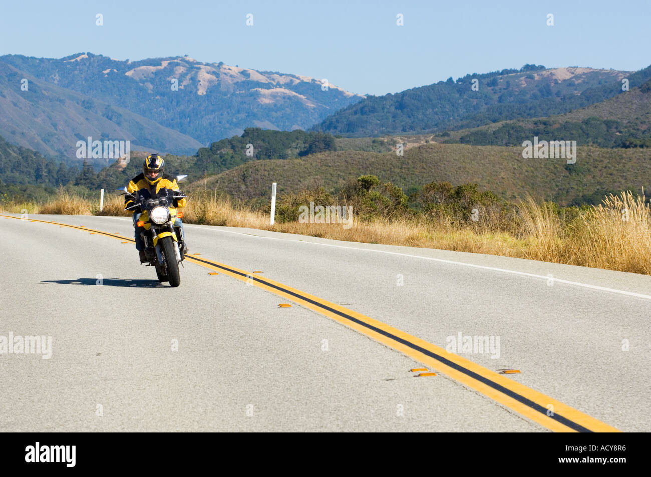 Single mature female motorcyclist rides motorcycle along pacific coast ...