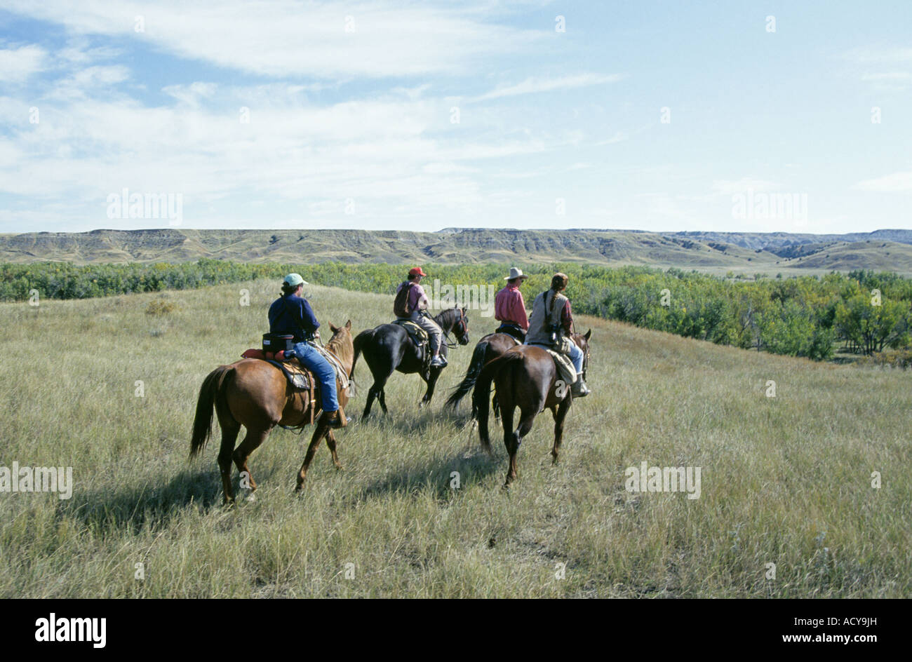 Horseback riders explore the eroded mud cliffs and mesas of Bandlands ...
