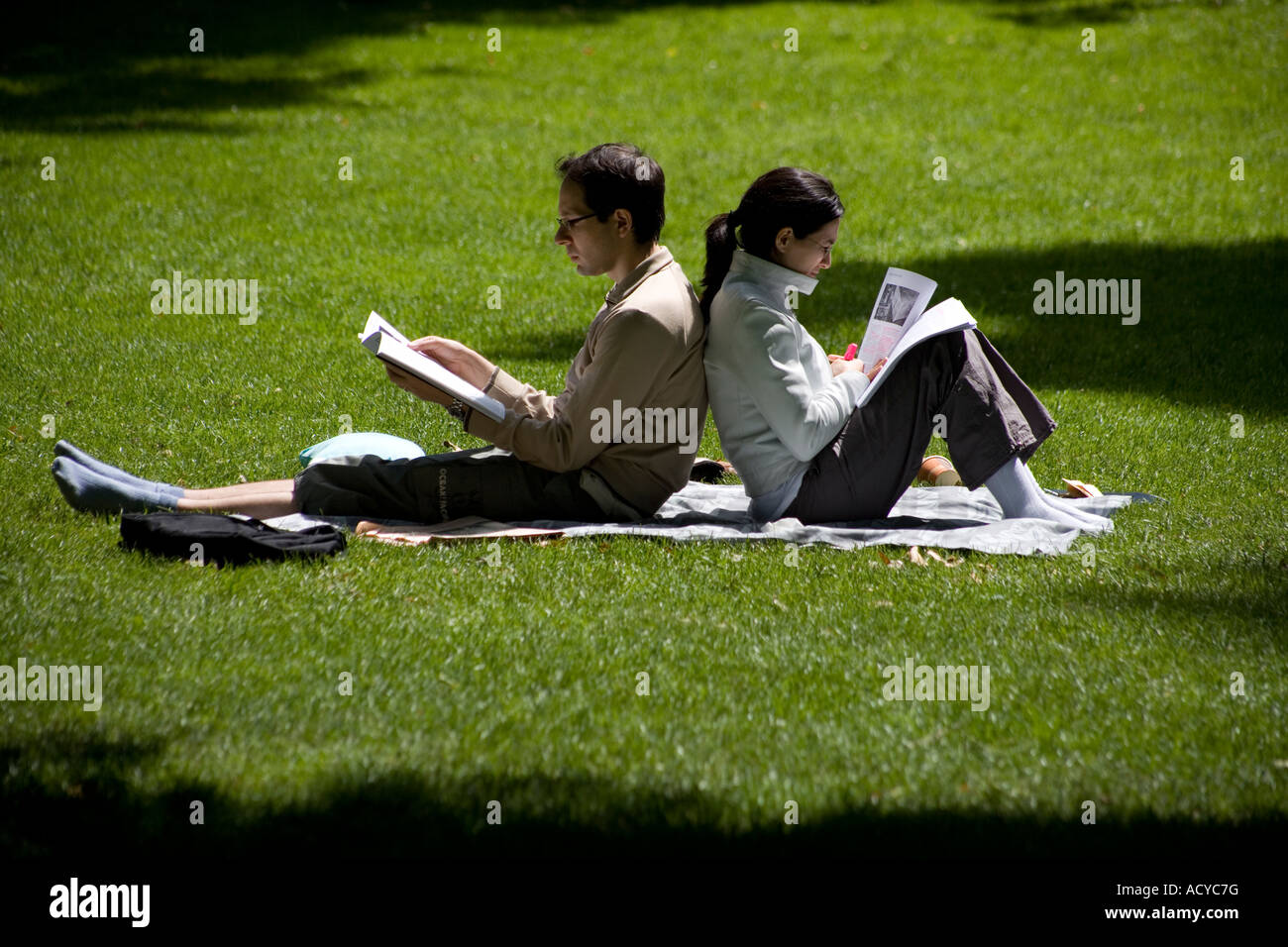 Young Couple sitting back to back reading in St James Park London ...