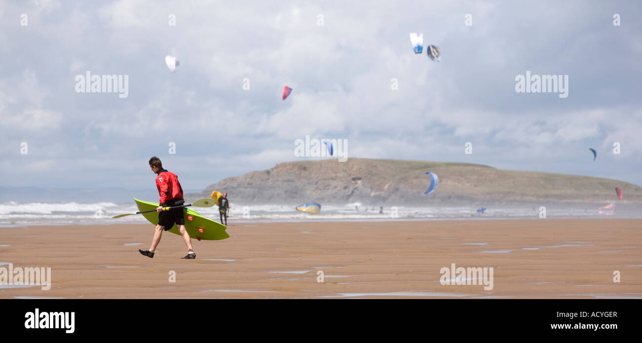 Man carrying sea kayak on beach with kites in background Stock Photo ...