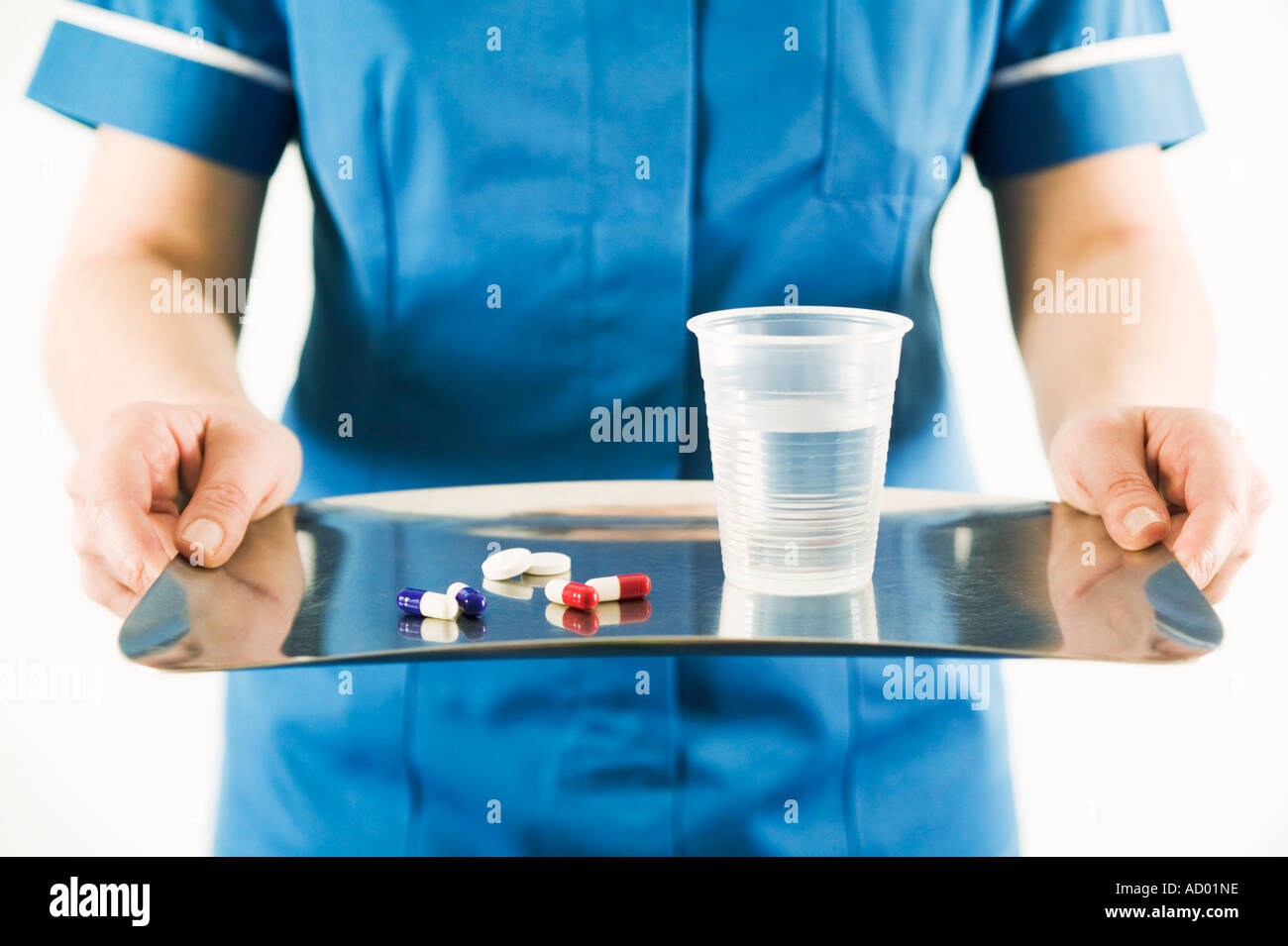 nurse wearing blue uniform holding tray with medication and a glass of ...