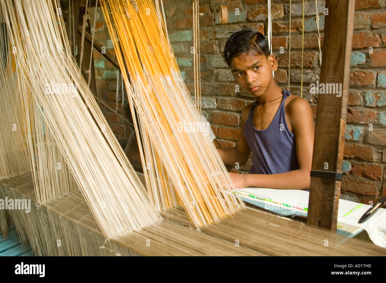 Horizontal portrait of a thin young boy working at a loom making silk ...