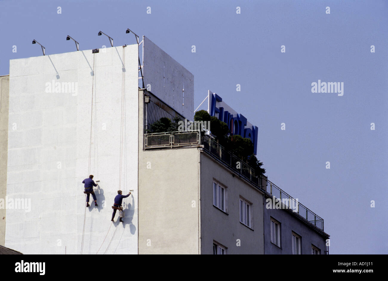 Workmen painting over a billboard on the side of a residential tower ...
