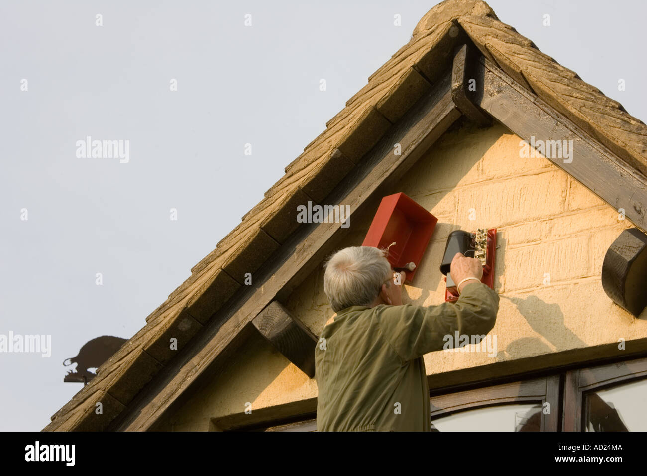 Electrical engineer on roof ladder testing burglar alarm unit Cotswolds ...